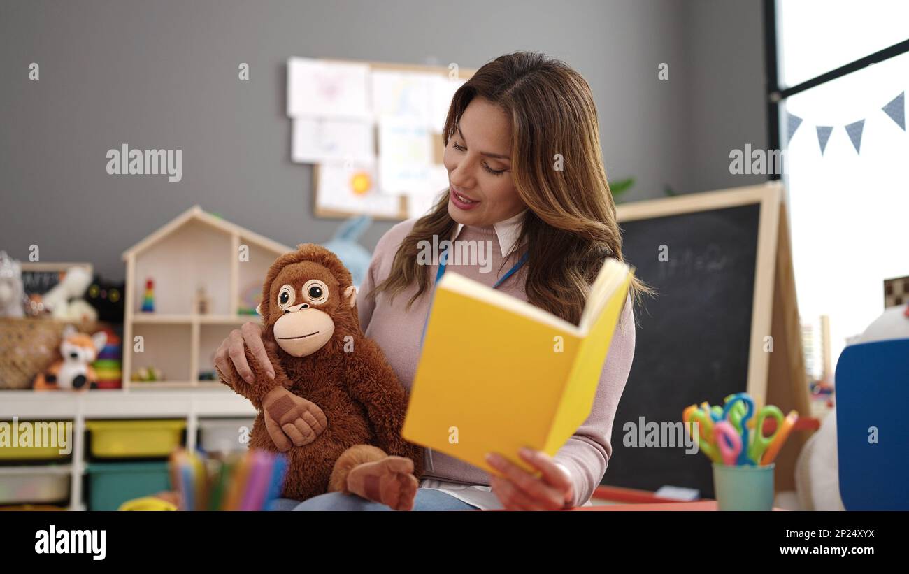 Young beautiful hispanic woman preschool teacher reading story book at ...