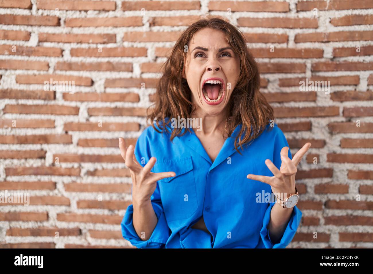 Beautiful brunette woman standing over bricks wall crazy and mad ...