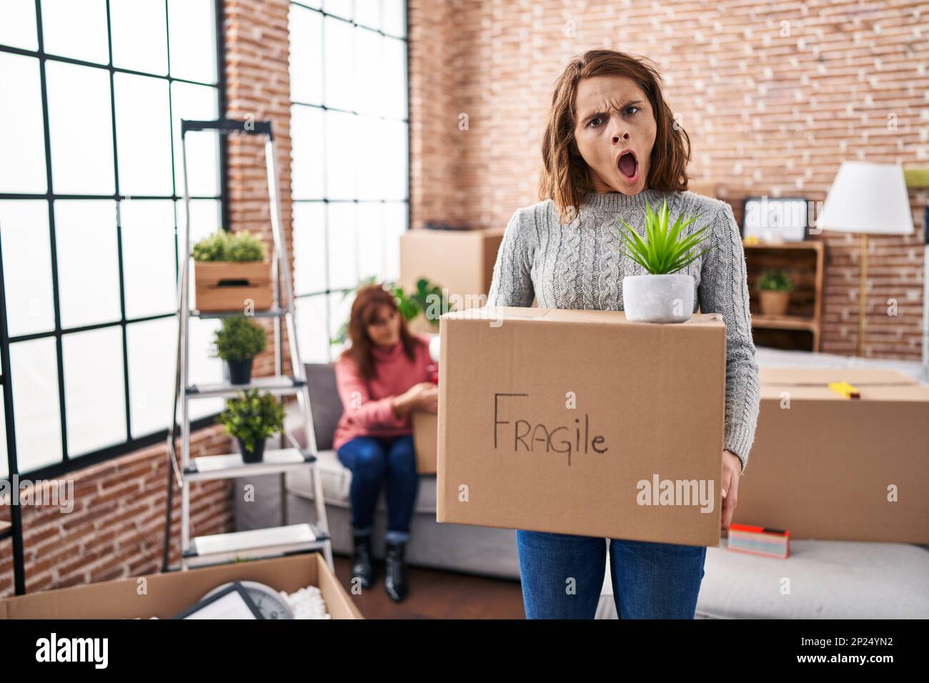 Mother and daughter moving to a new home holding cardboard box in shock ...