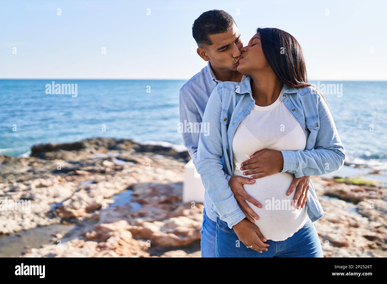 Young latin couple expecting baby hugging each other and kissing at seaside Stock Photo - Alamy