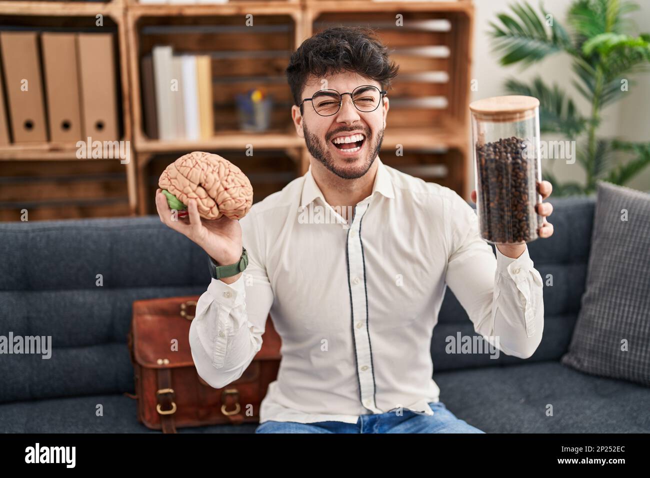 Hispanic man with beard working at therapy office holding brain and ...