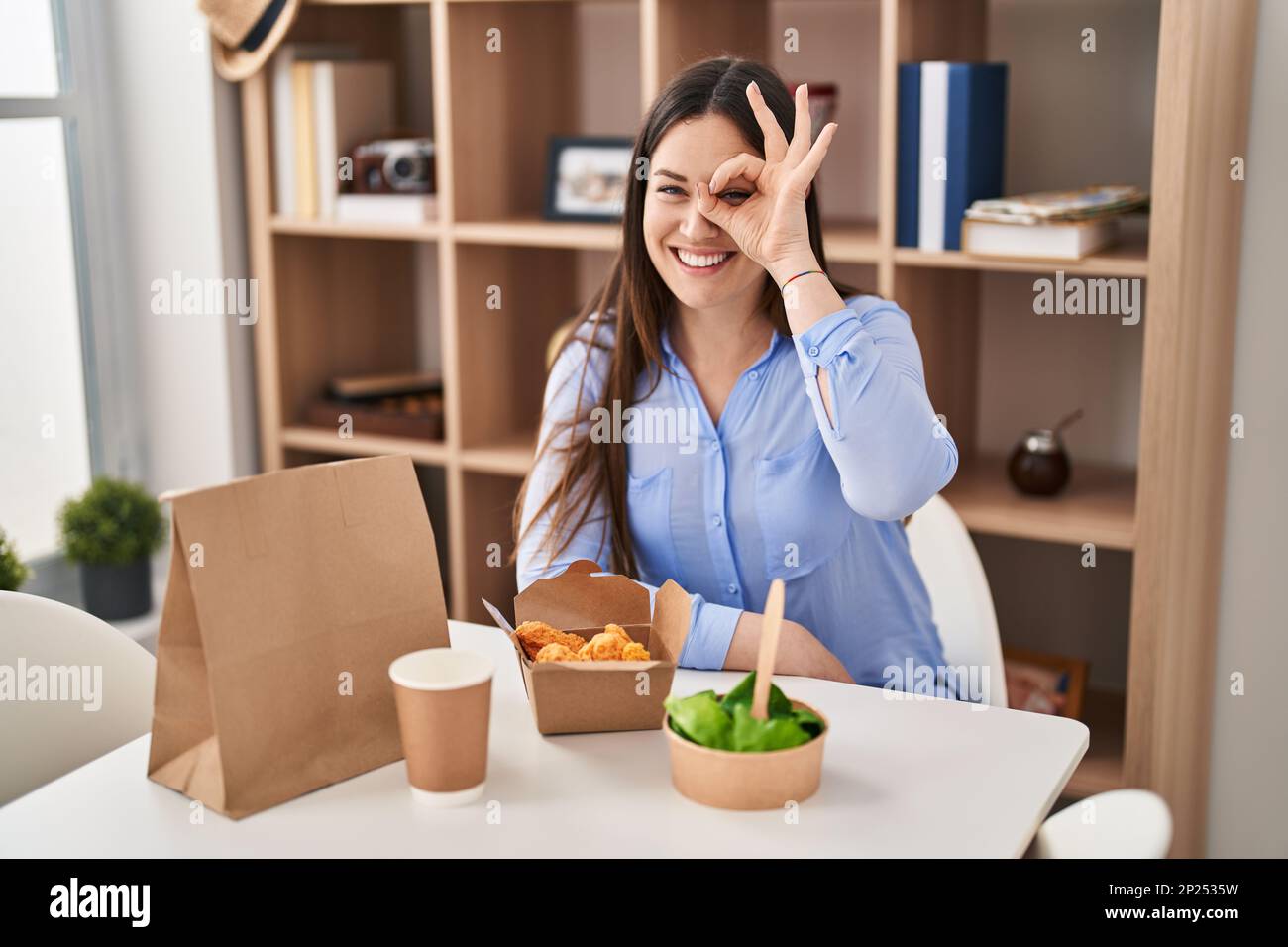 Young brunette woman eating take away food at home smiling happy doing ...