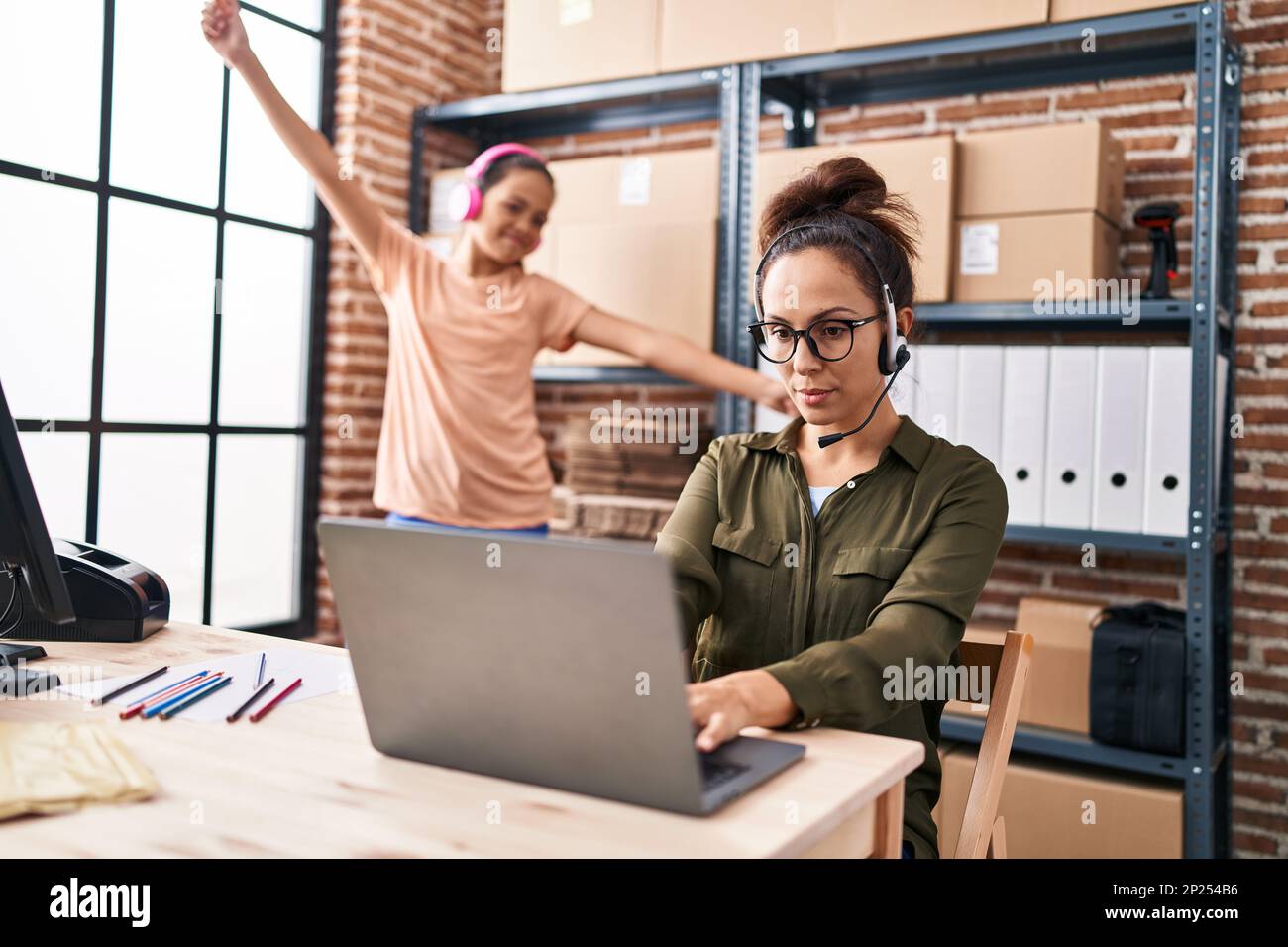 Woman and girl ecommerce call center agent working and daughter dancing ...