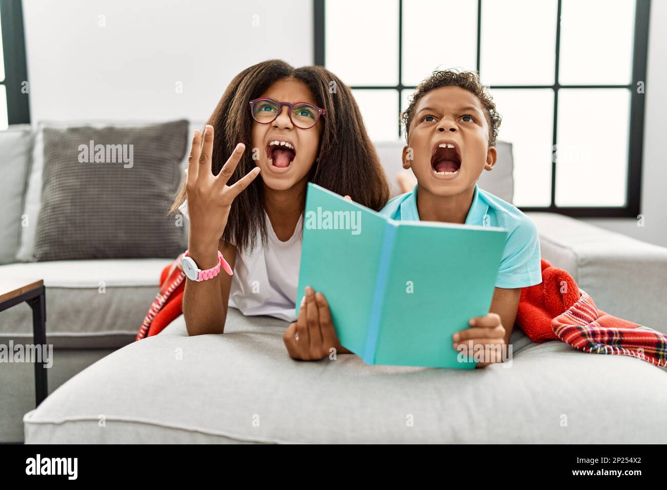 Two siblings lying on the sofa reading a book crazy and mad shouting ...