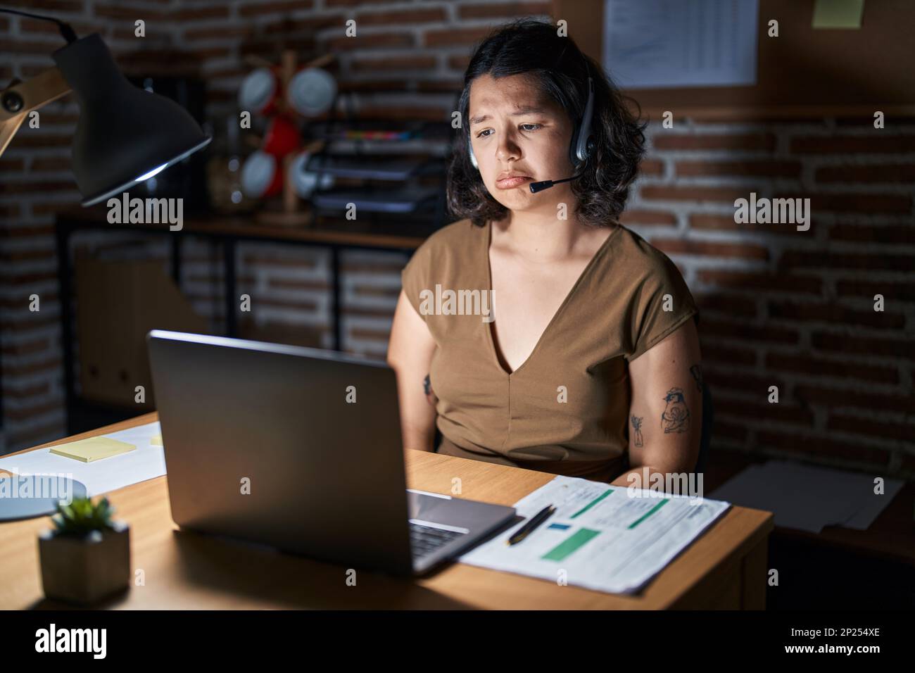 Young hispanic woman working at the office at night depressed and worry ...