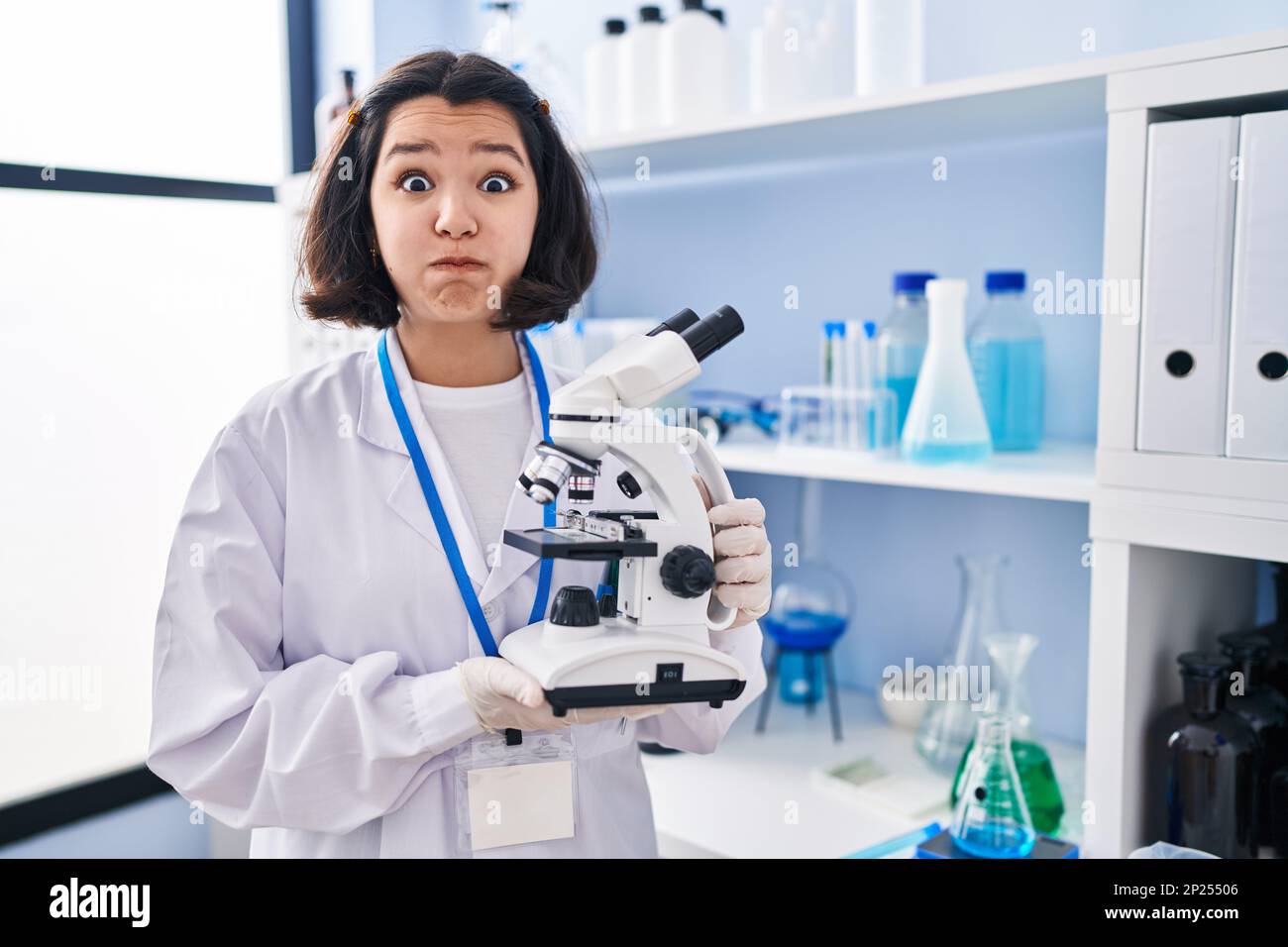 Young hispanic woman working at scientist laboratory holding microscope ...
