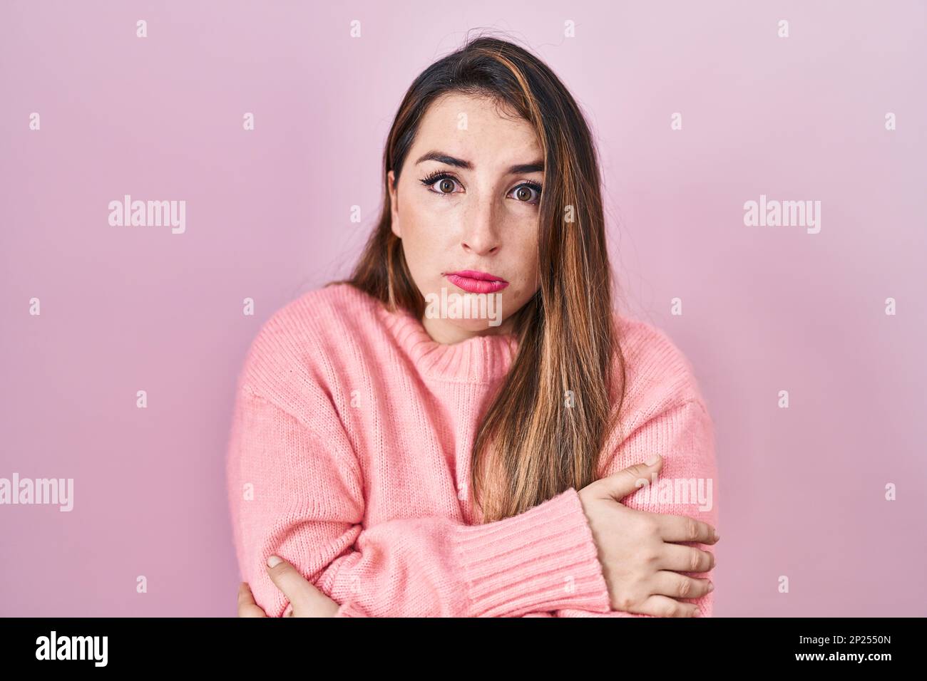 Young hispanic woman standing over pink background shaking and freezing ...