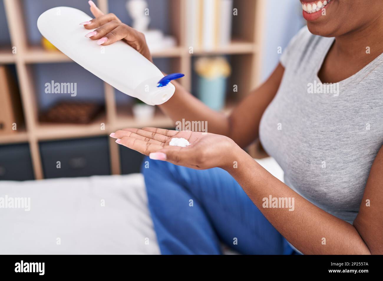 African american woman pouring lotion on hand sitting on bed at bedroom ...