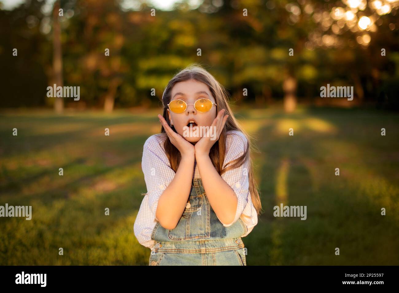 surprised and excited school girl on lawn with green trees background ...