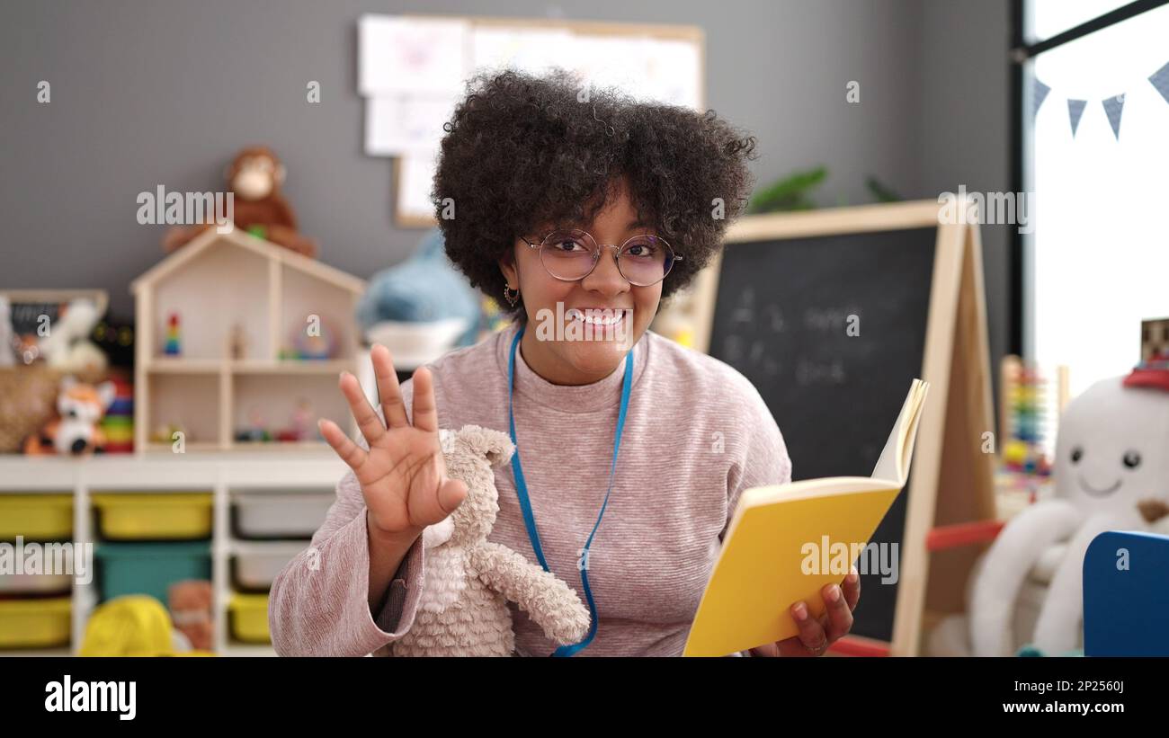Young african american woman preschool teacher reading story book at ...