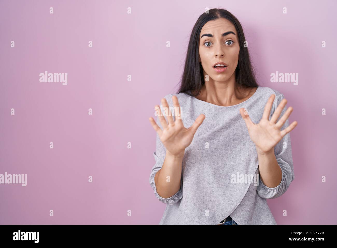 Young brunette woman standing over pink background afraid and terrified ...