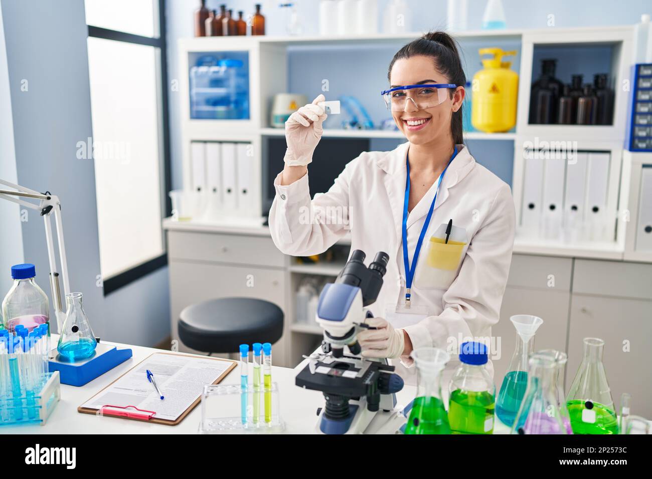 Young beautiful hispanic woman scientist using microscope holding sample at laboratory Stock ...