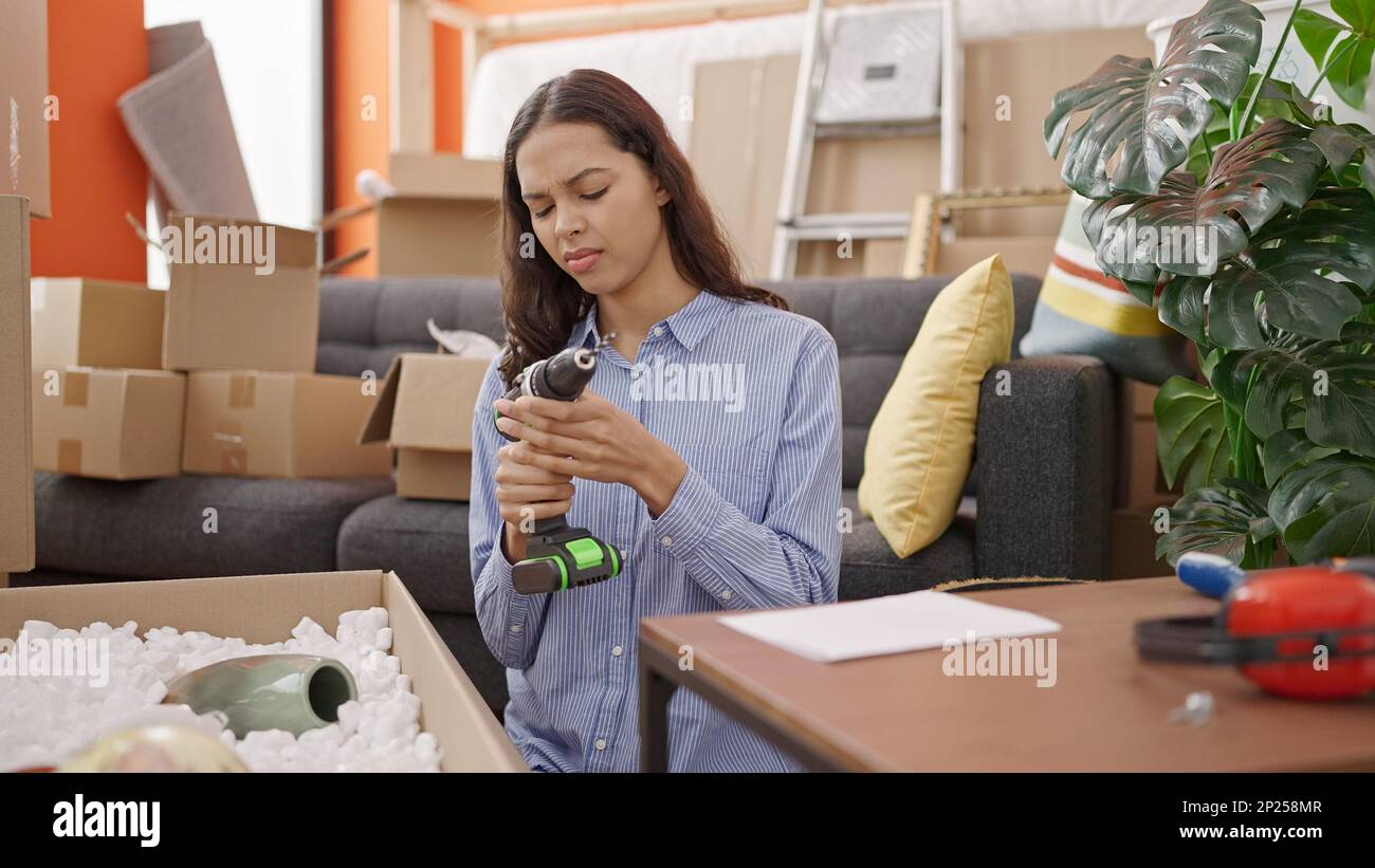 Young beautiful hispanic woman assembling new table using drill at new ...