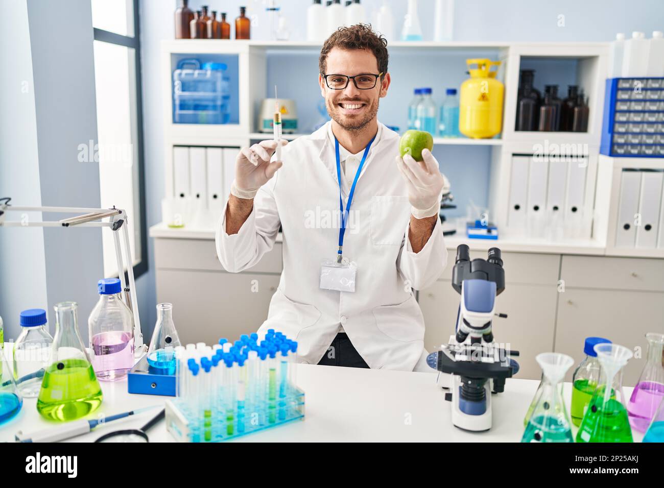 Young hispanic man working at scientist laboratory holding apple ...