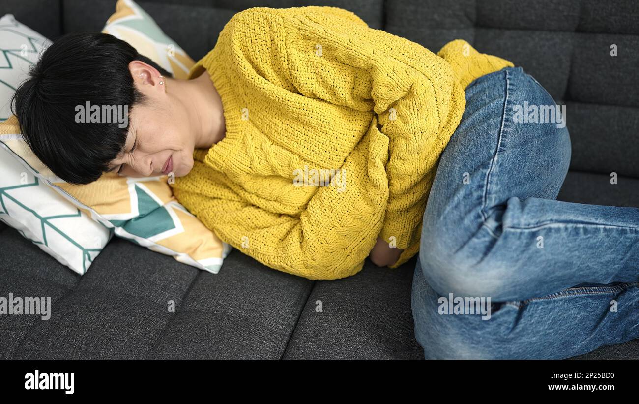 Young chinese woman suffering for stomach ache lying on sofa at home ...