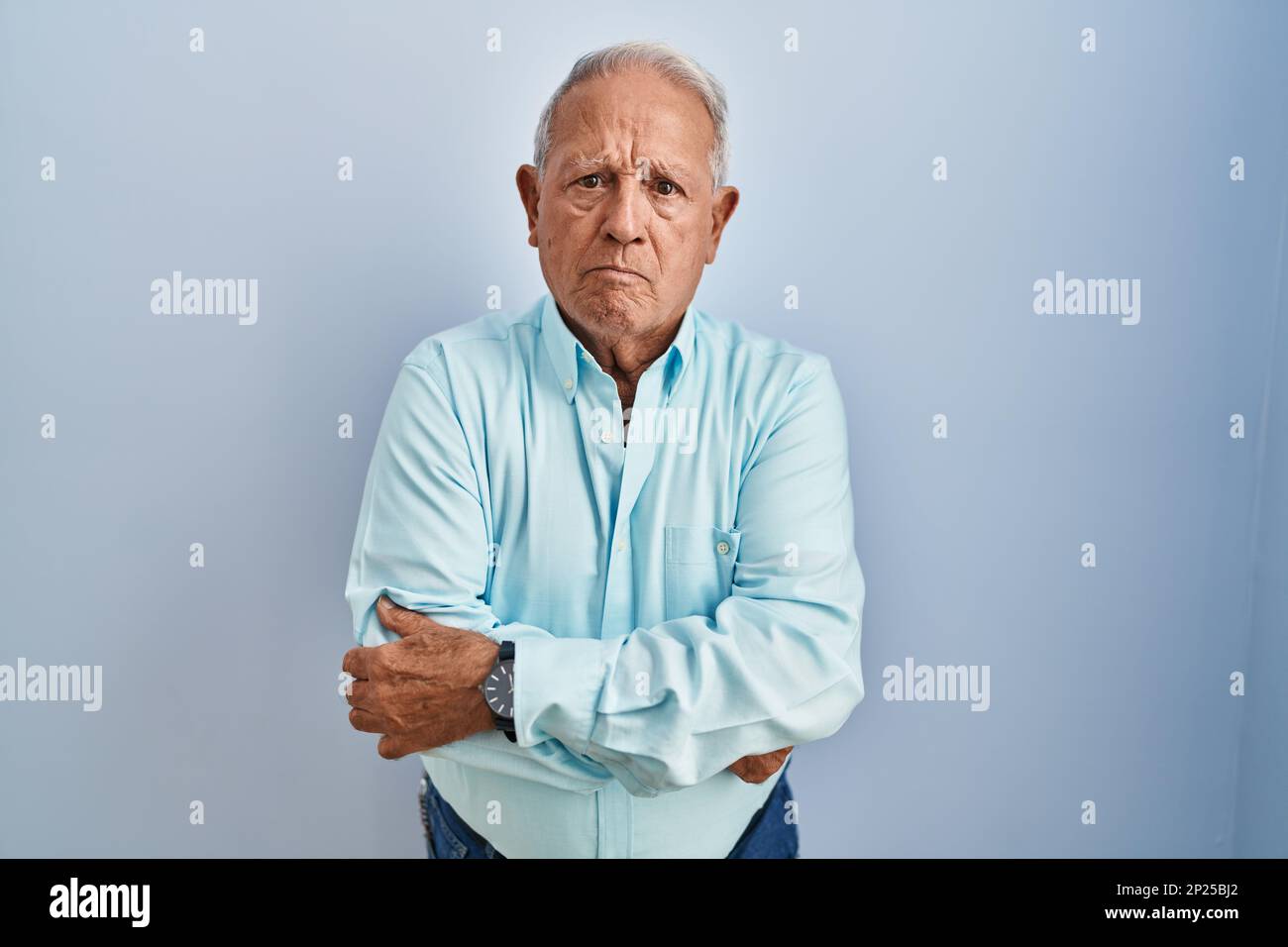 Senior man with grey hair standing over blue background skeptic and ...