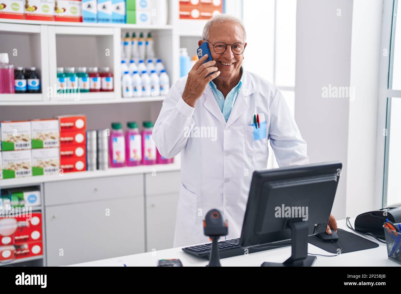 Senior grey-haired man pharmacist talking on smartphone using computer ...