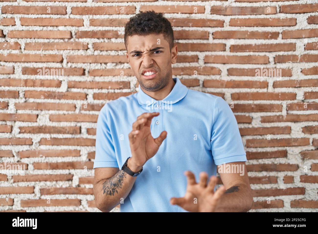 Brazilian young man standing over brick wall disgusted expression ...