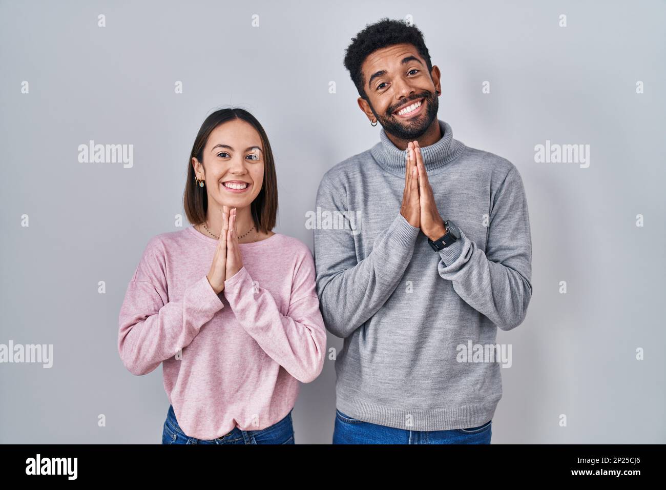 Young hispanic couple standing together praying with hands together ...