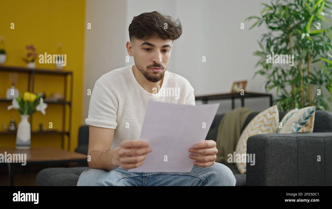 Young arab man reading paper sitting on sofa at home Stock Photo - Alamy
