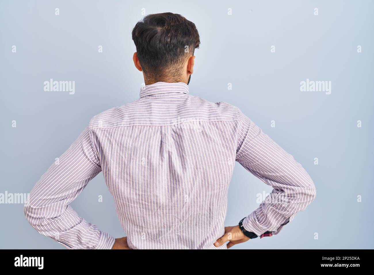 Arab man with beard standing over blue background standing backwards ...
