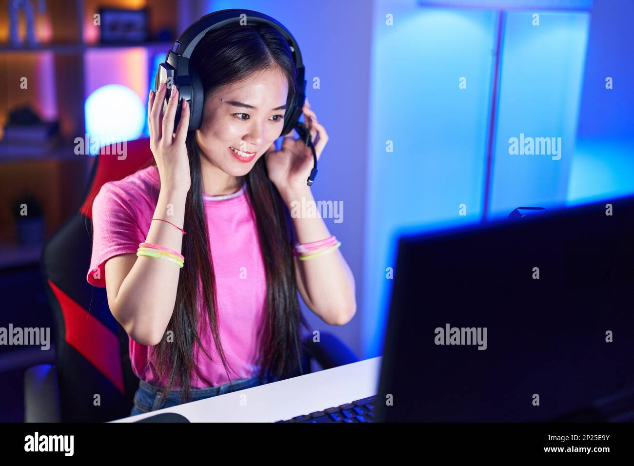 Young chinese woman streamer smiling confident sitting on bed at gaming ...
