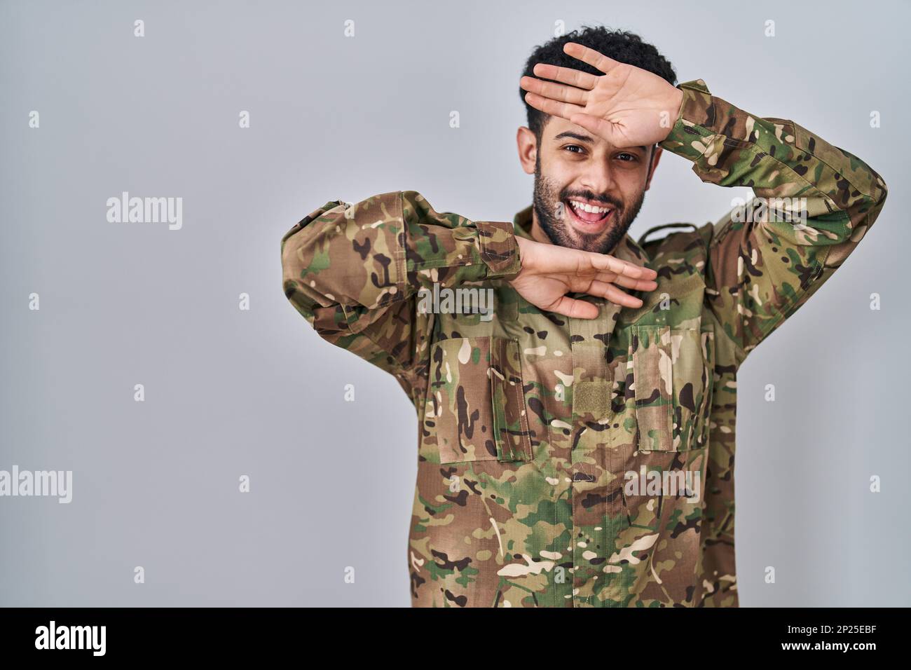 Arab man wearing camouflage army uniform smiling cheerful playing peek ...