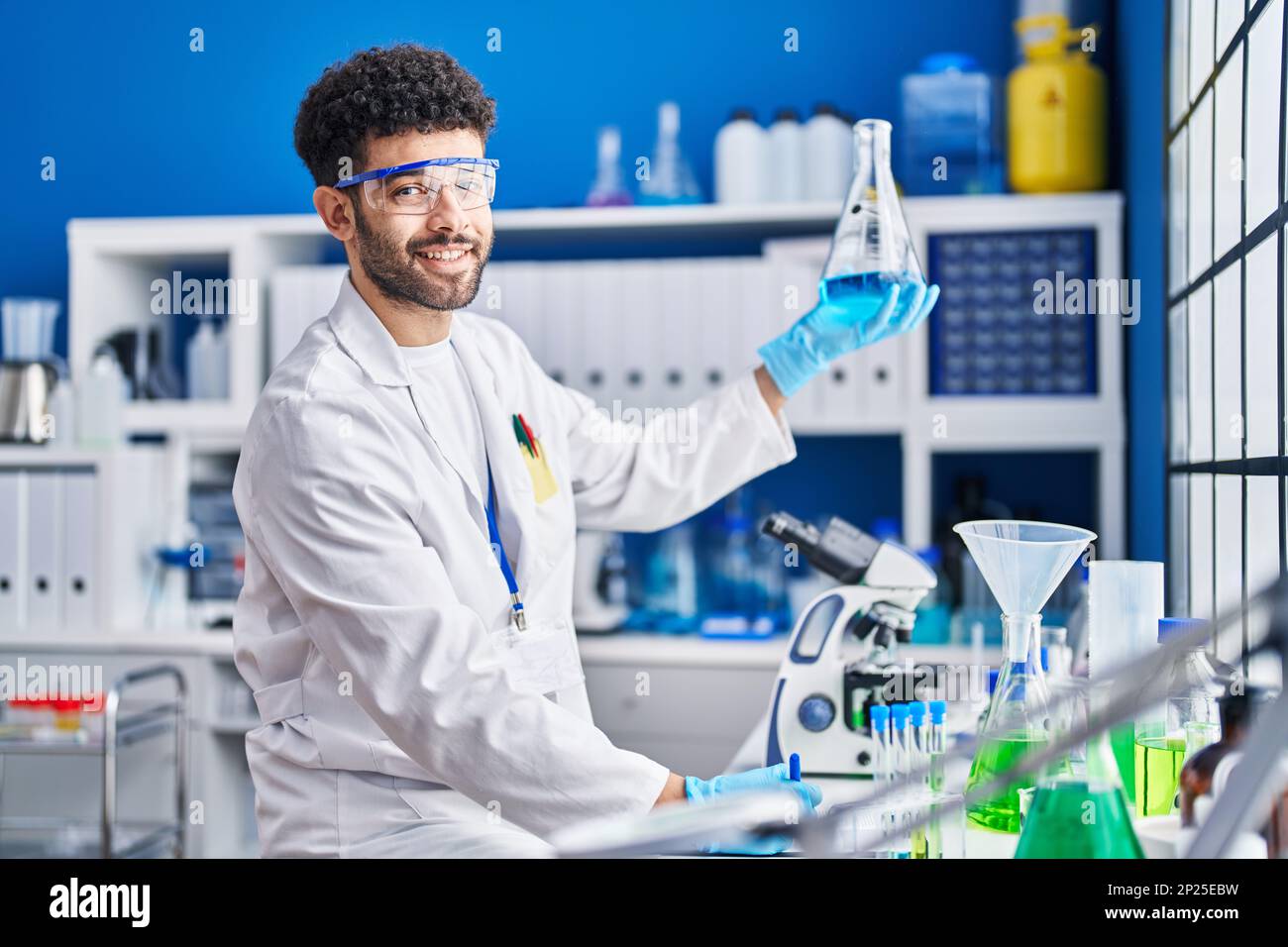 Young arab man wearing scientist uniform measuring liquid at laboratory ...