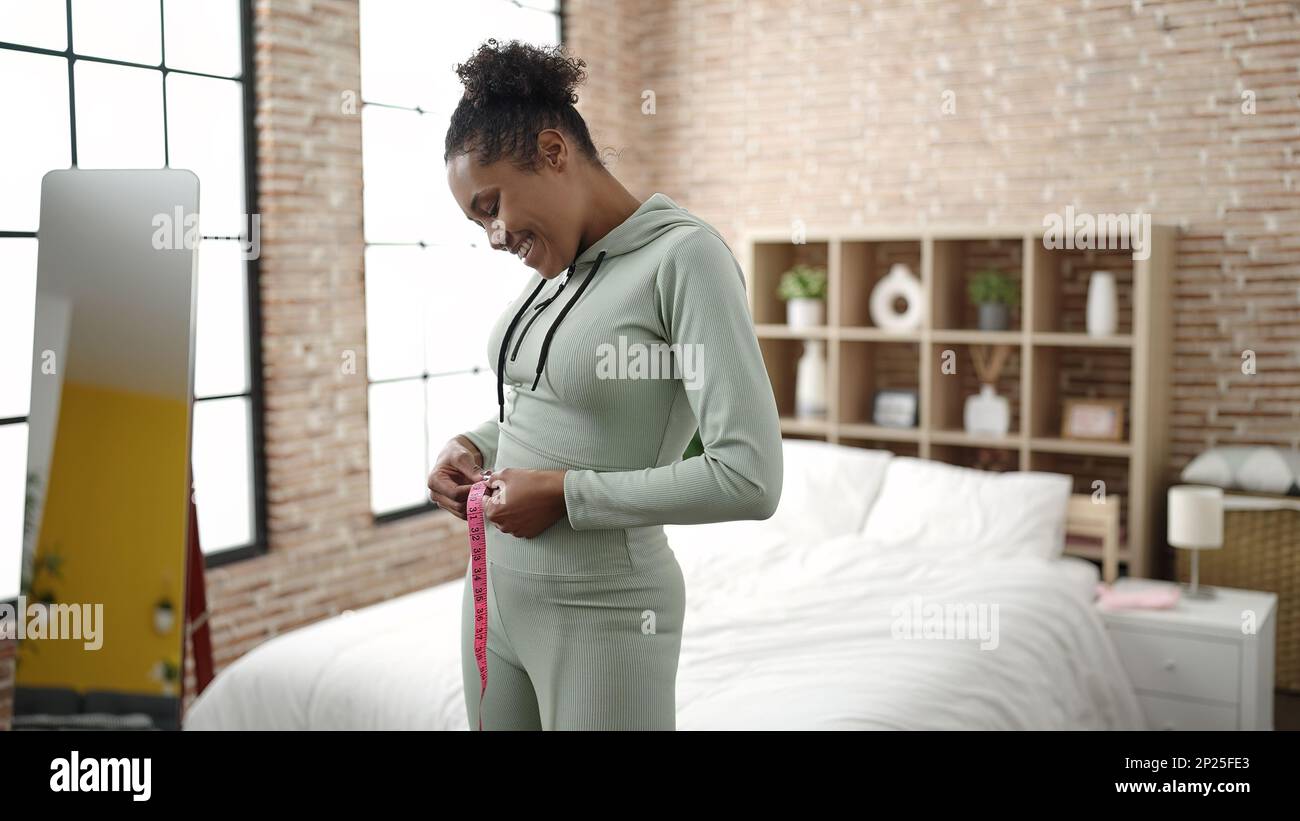 African american woman smiling confident measuring abdomen with tape ...