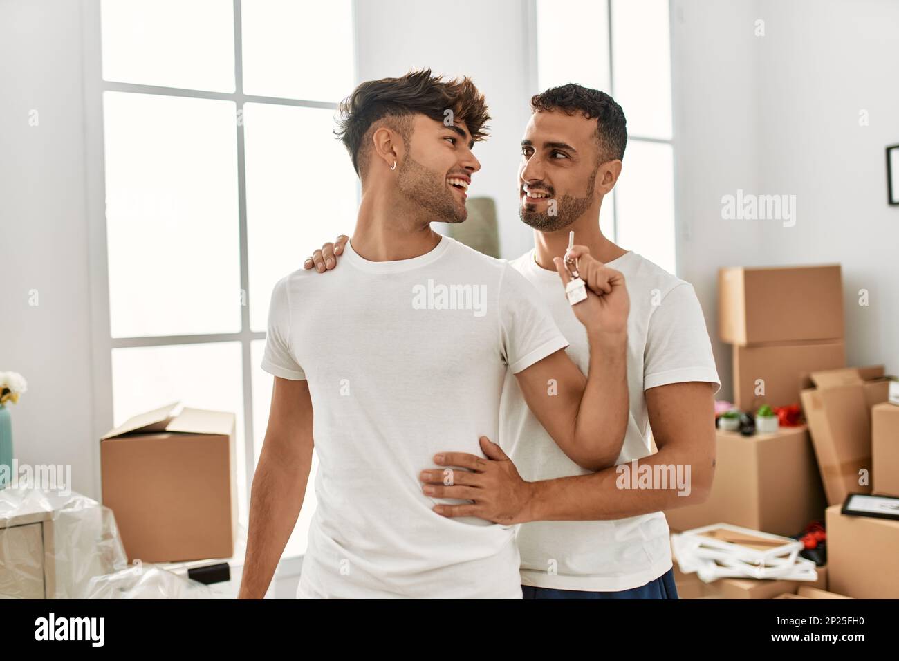 Two hispanic men couple hugging each other holding key of new house at ...