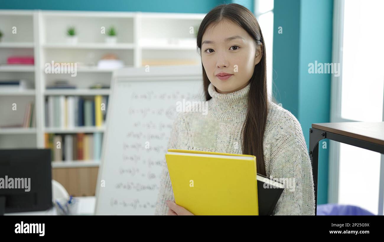 Young chinese woman student holding books standing with relaxed ...