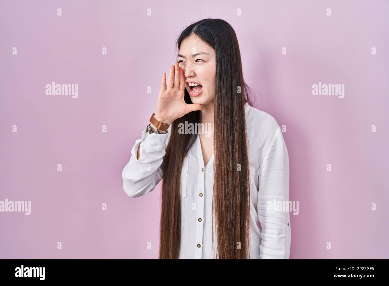 Chinese young woman standing over pink background shouting and ...