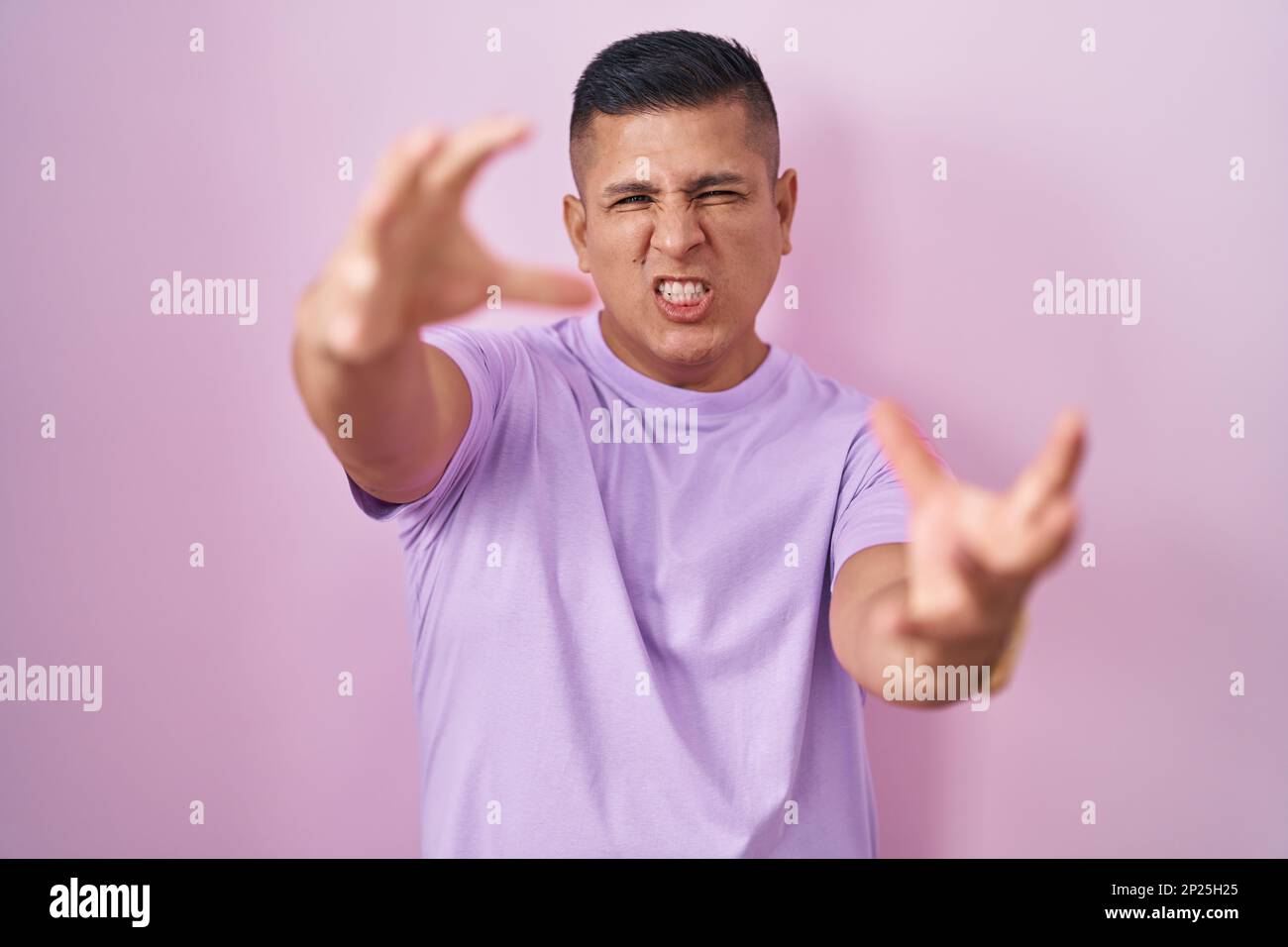 Young hispanic man standing over pink background shouting frustrated ...