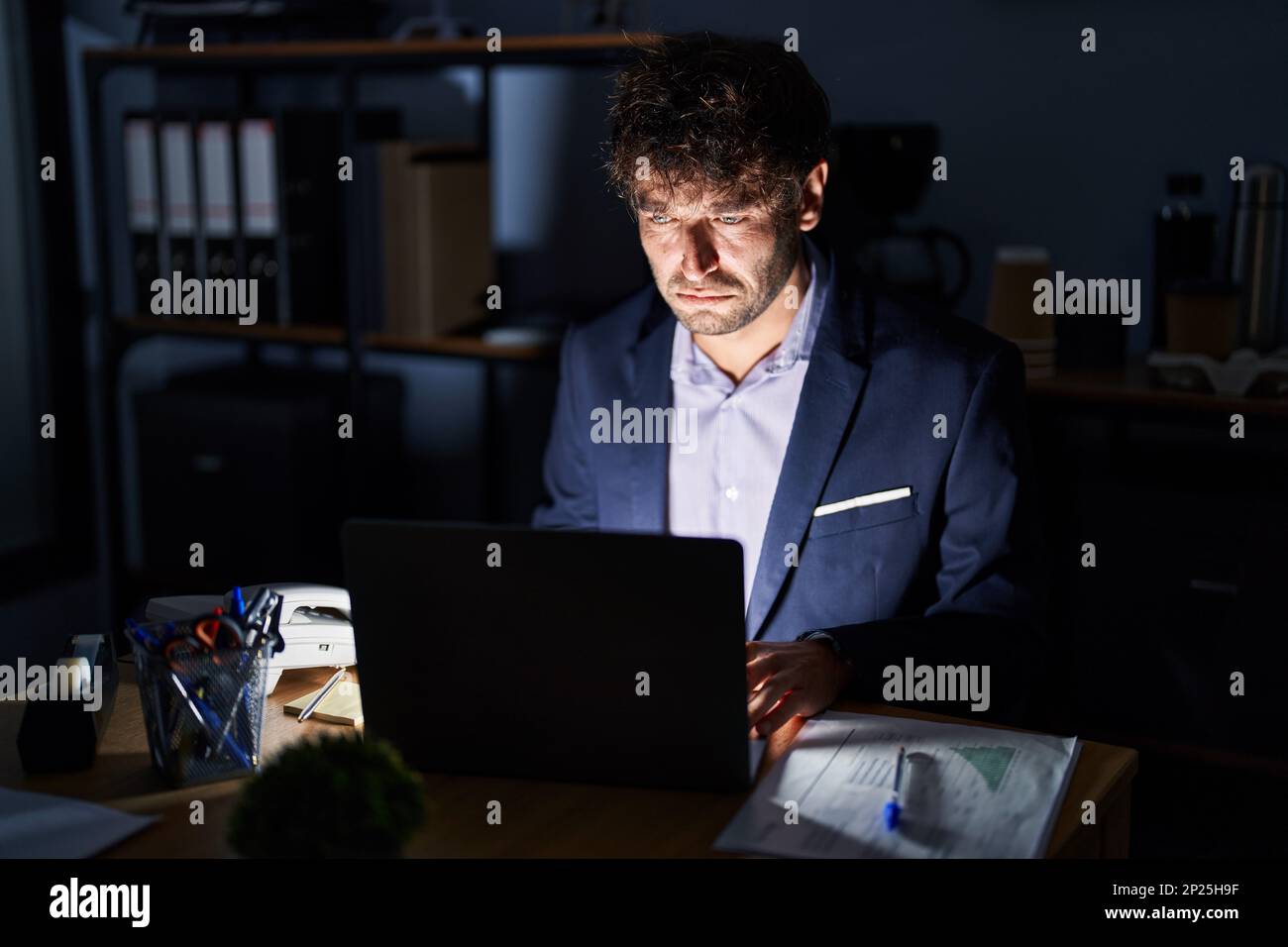 Hispanic young man working at the office at night depressed and worry ...