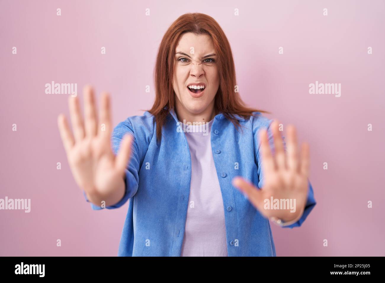 Young hispanic woman with red hair standing over pink background doing ...