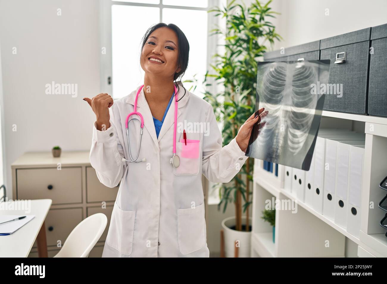 Young asian doctor woman holding chest x-ray pointing thumb up to the ...