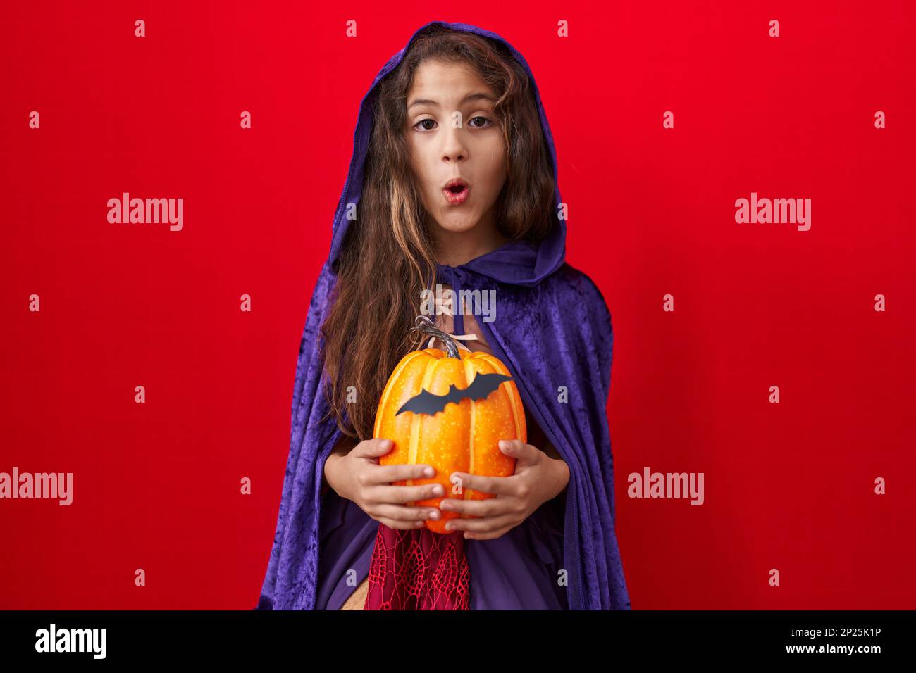 Little hispanic girl wearing witch halloween costume scared and amazed ...