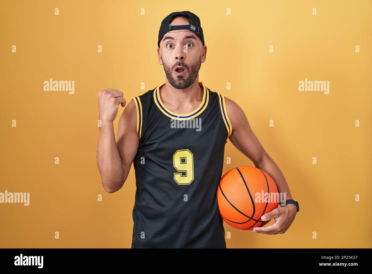 Middle age bald man holding basketball ball over yellow background ...