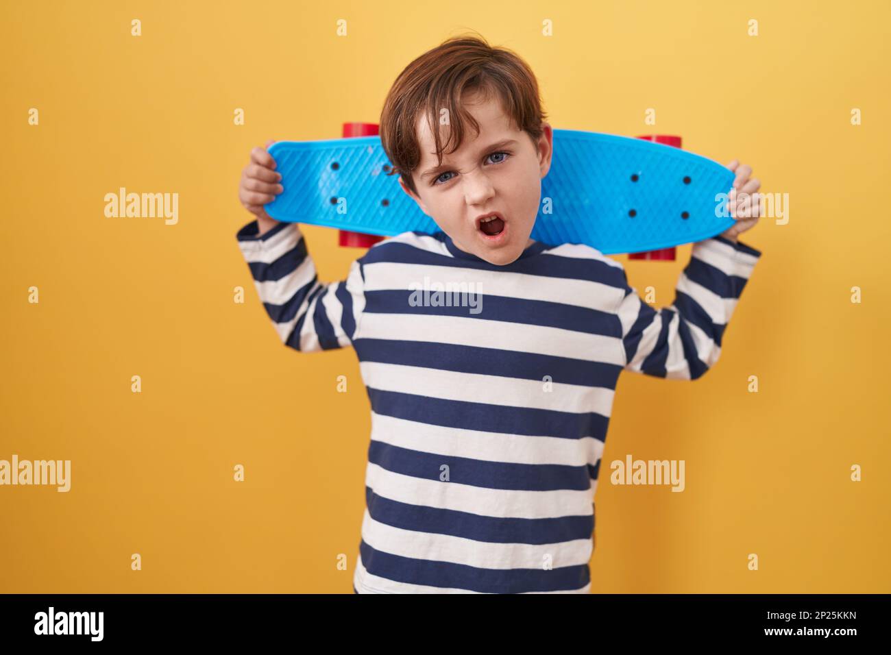 Little caucasian boy holding skate over yellow background in shock face ...