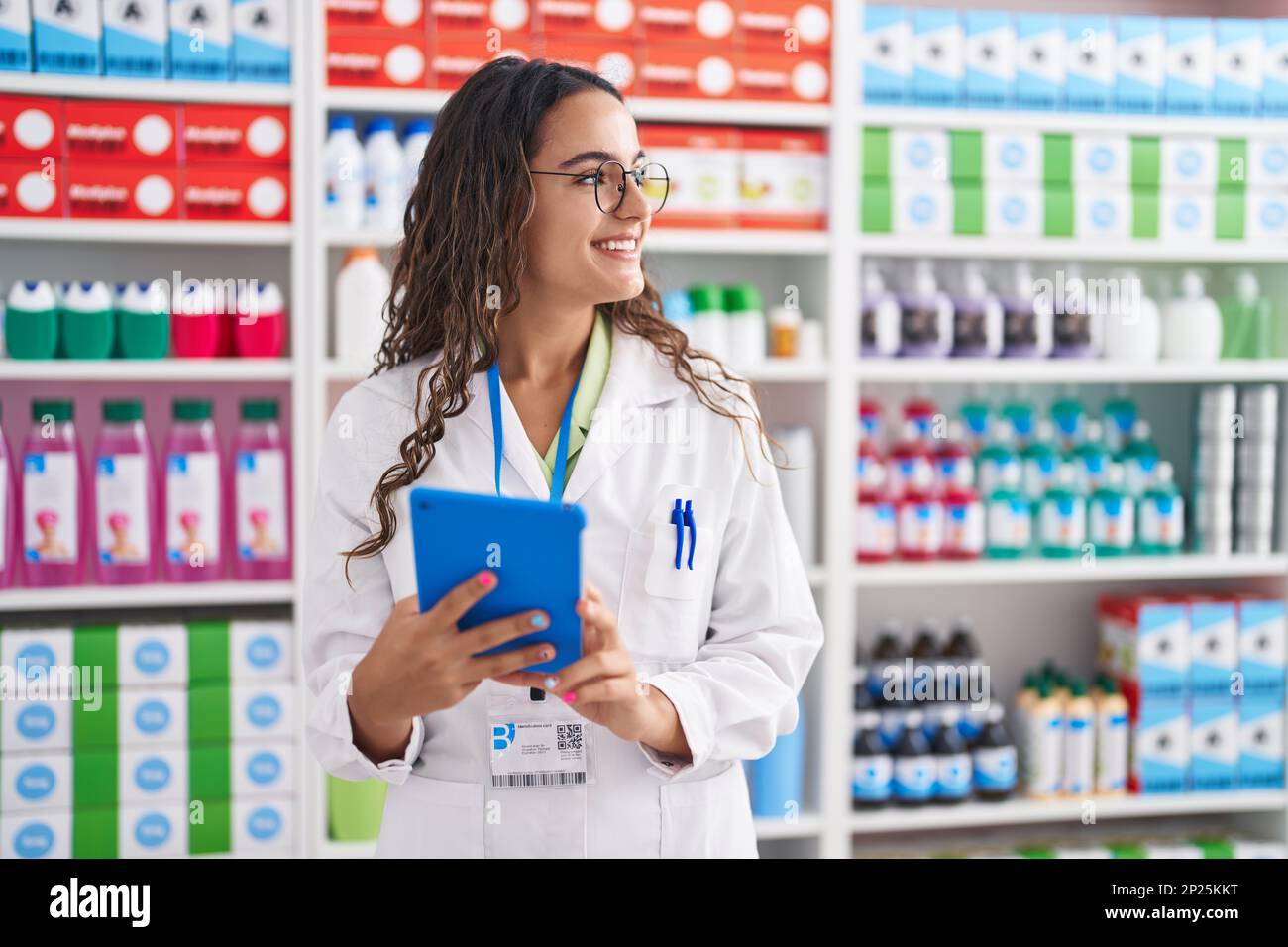 Young beautiful hispanic woman pharmacist using touchpad working at ...