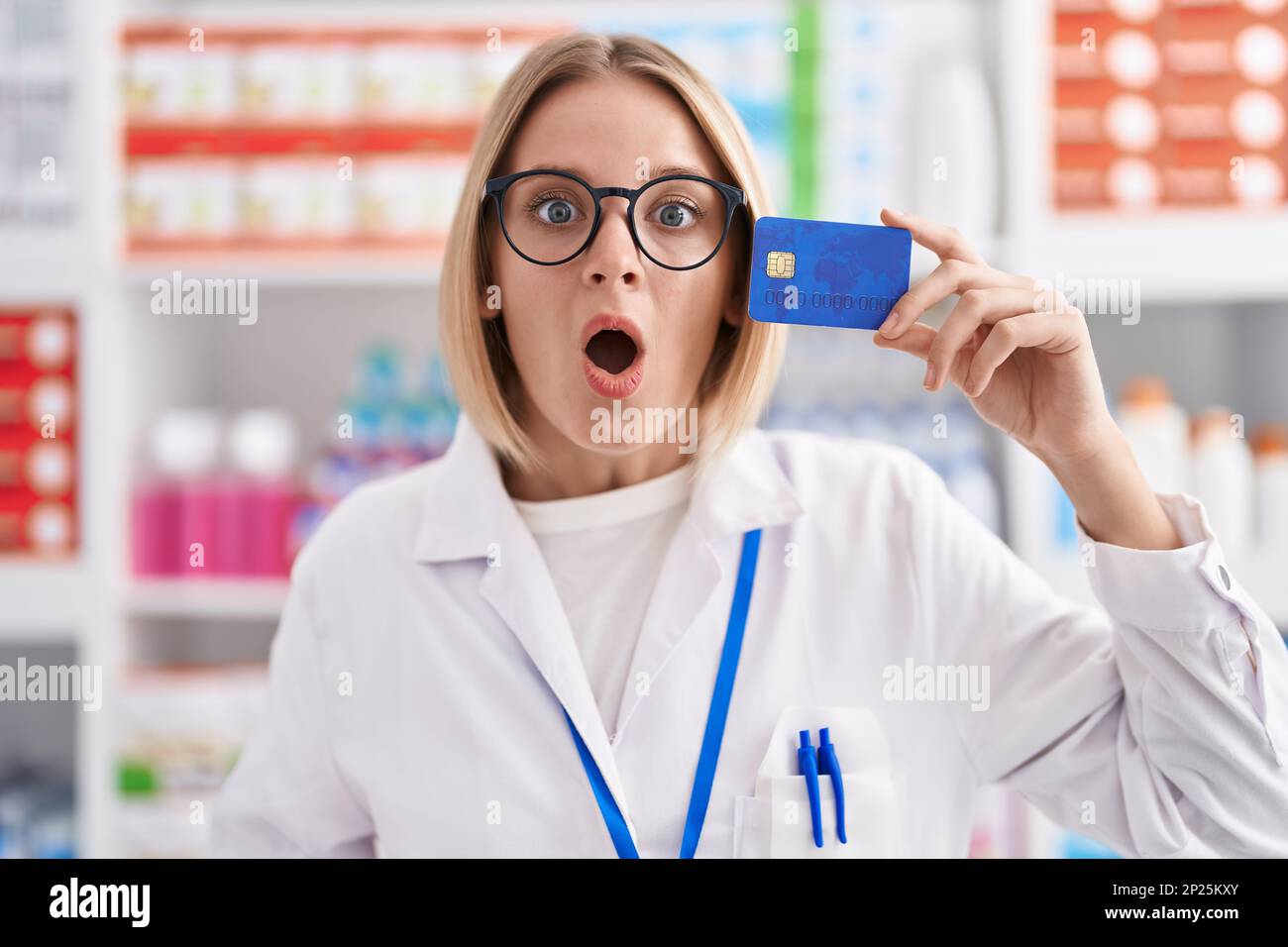 Young caucasian woman working at pharmacy drugstore holding credit card ...