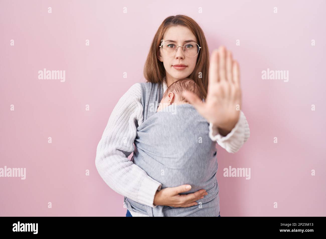 Young caucasian woman holding and carrying baby on a sling with open ...