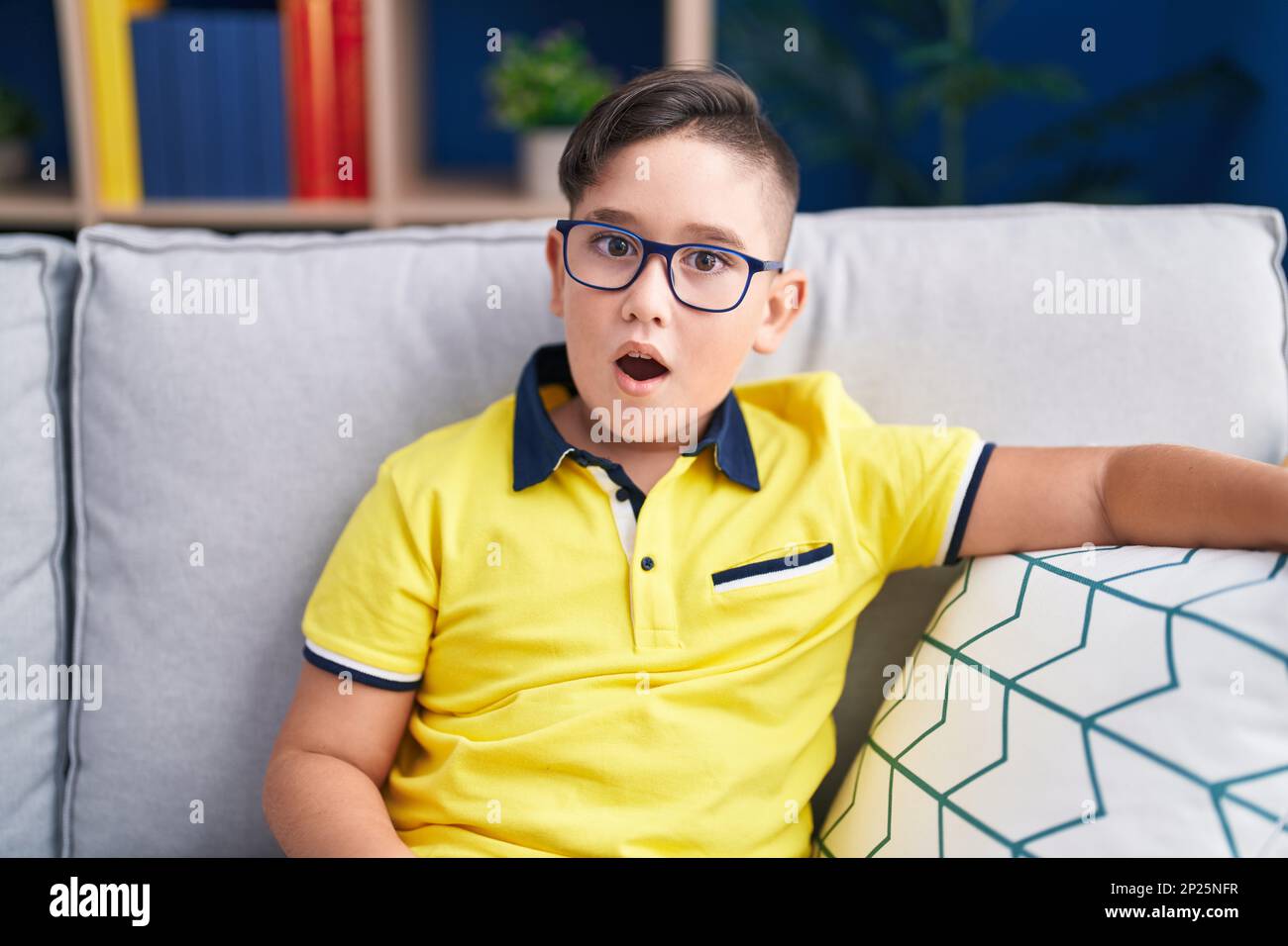 Young hispanic kid sitting on the sofa at home scared and amazed with ...