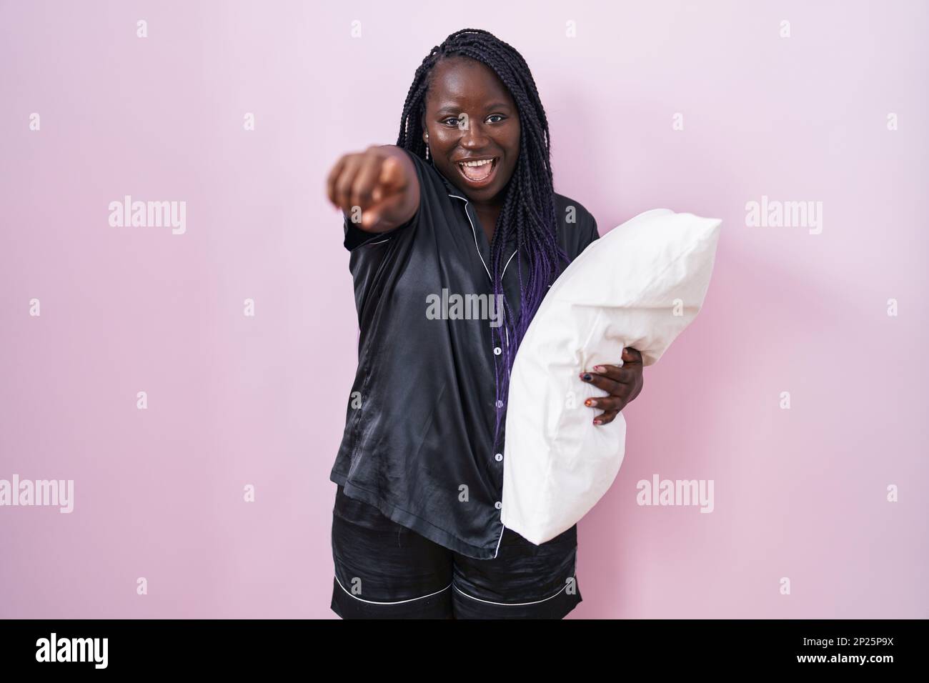 Young african woman wearing pijama hugging pillow pointing to you and ...