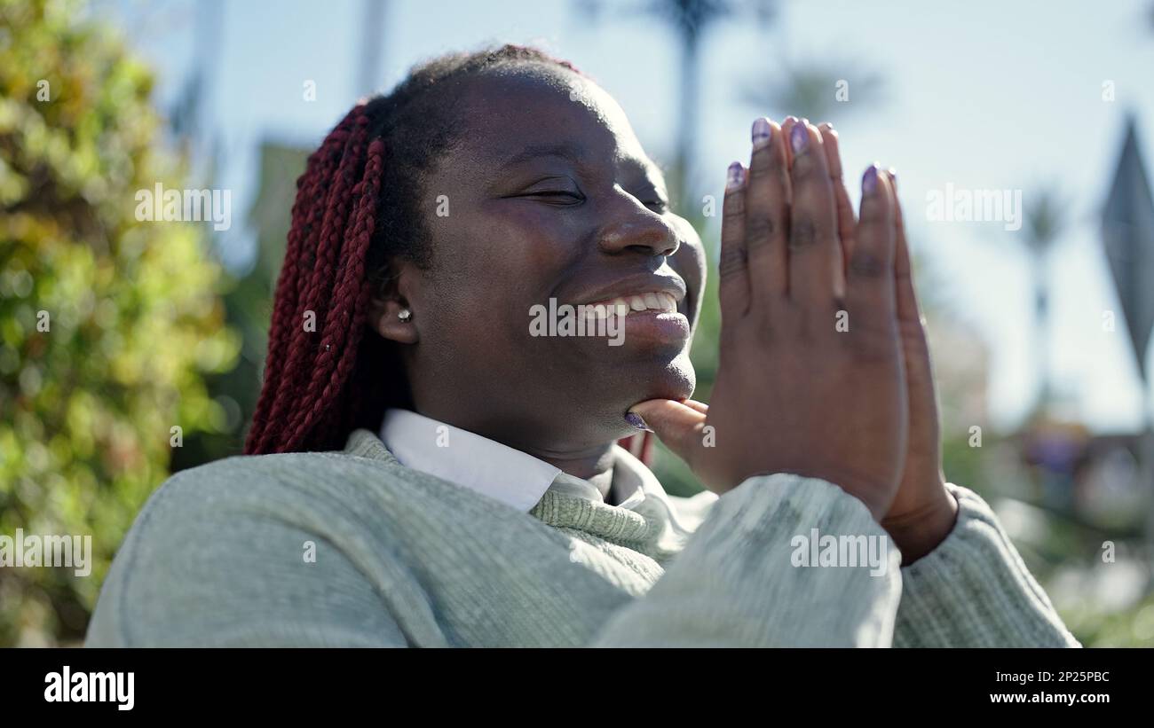 African woman with braided hair praying with closed eyes at park Stock ...