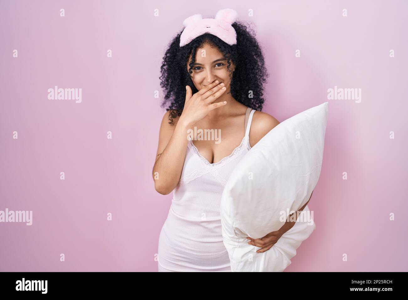 Hispanic woman with curly hair wearing sleep mask and pajama holding ...