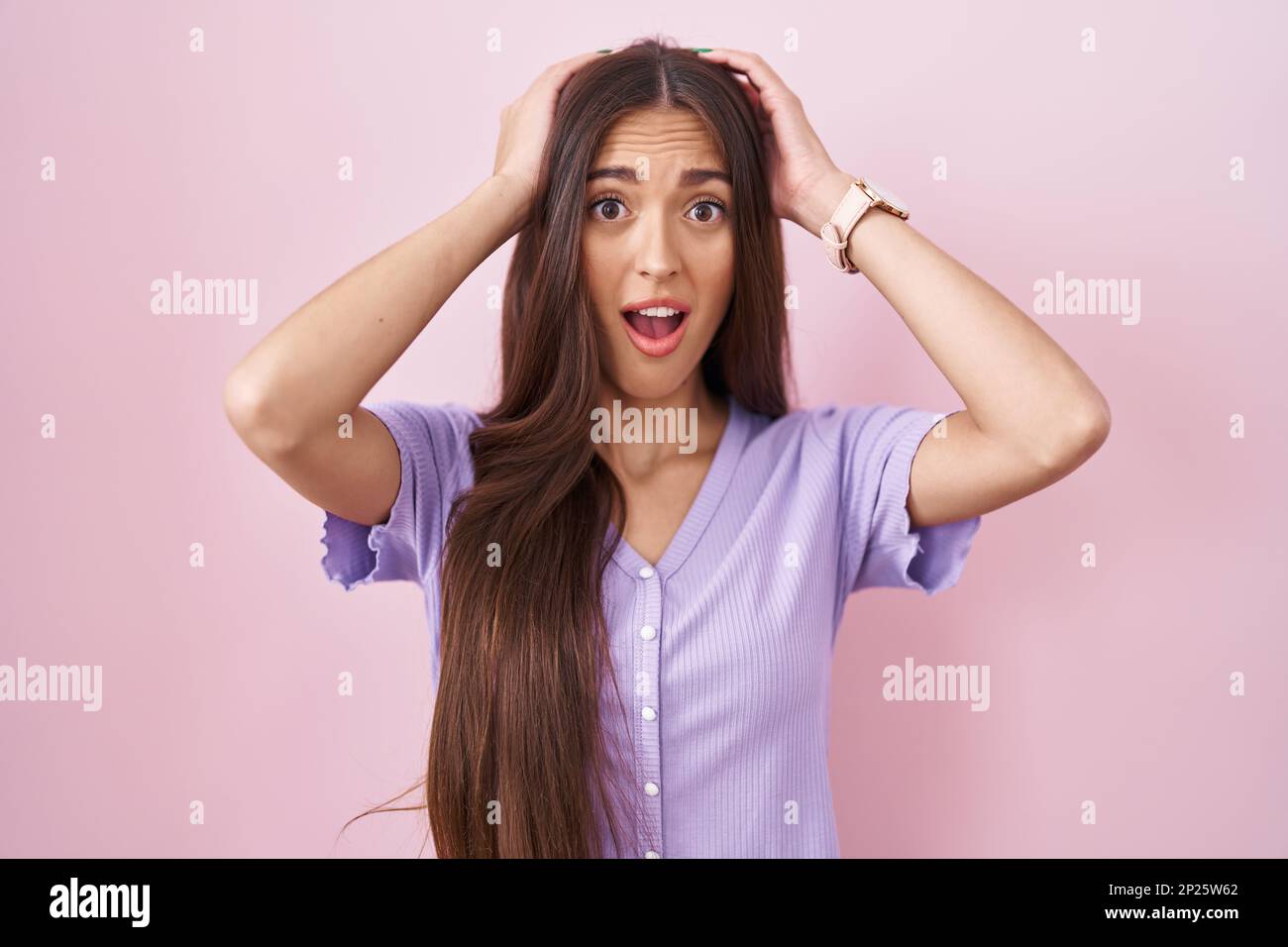 Young hispanic woman with long hair standing over pink background crazy ...