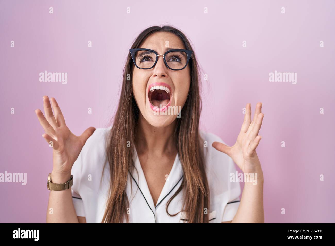 Young brunette woman wearing glasses standing over pink background ...