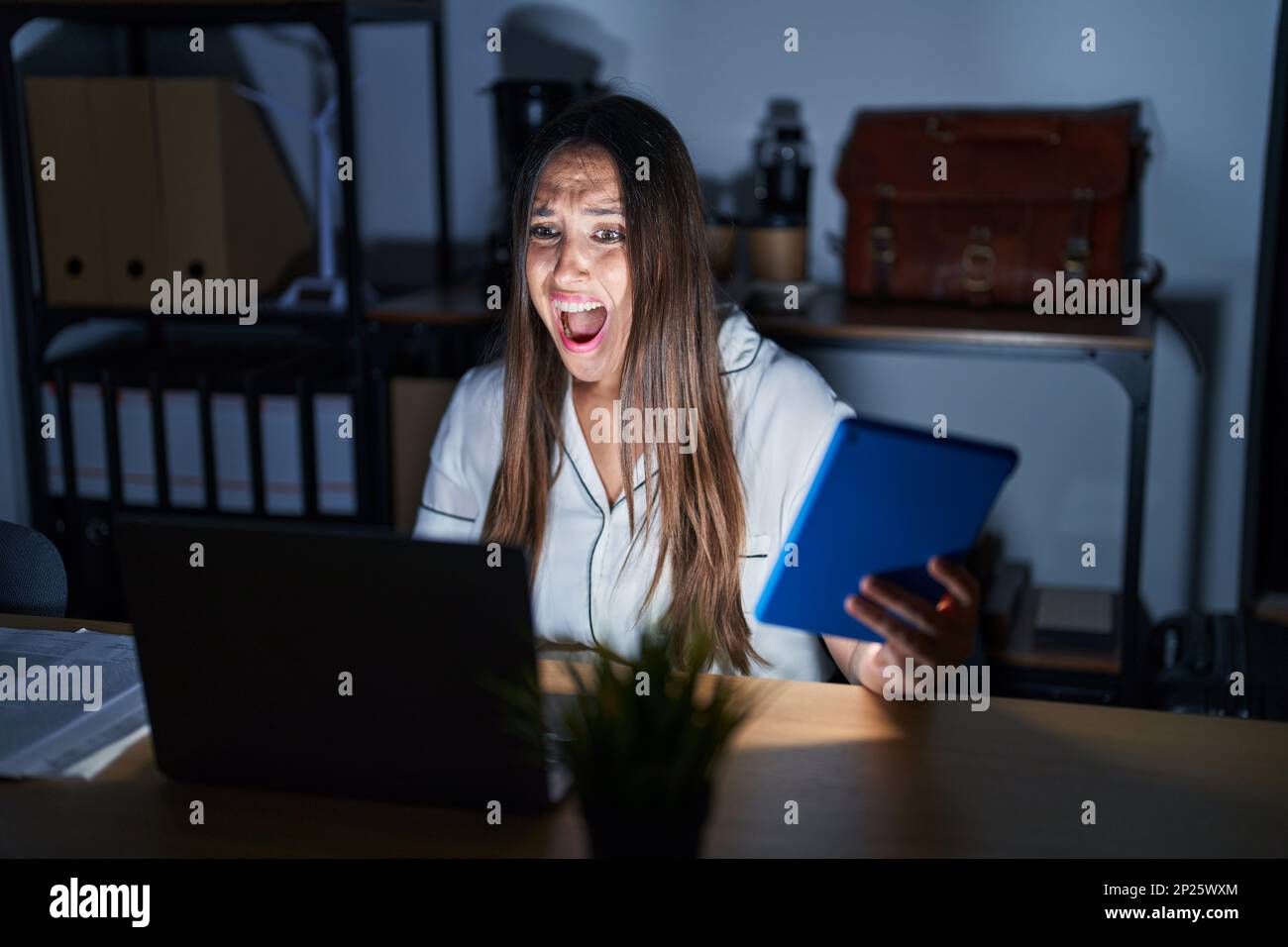 Young brunette woman working at the office at night angry and mad ...