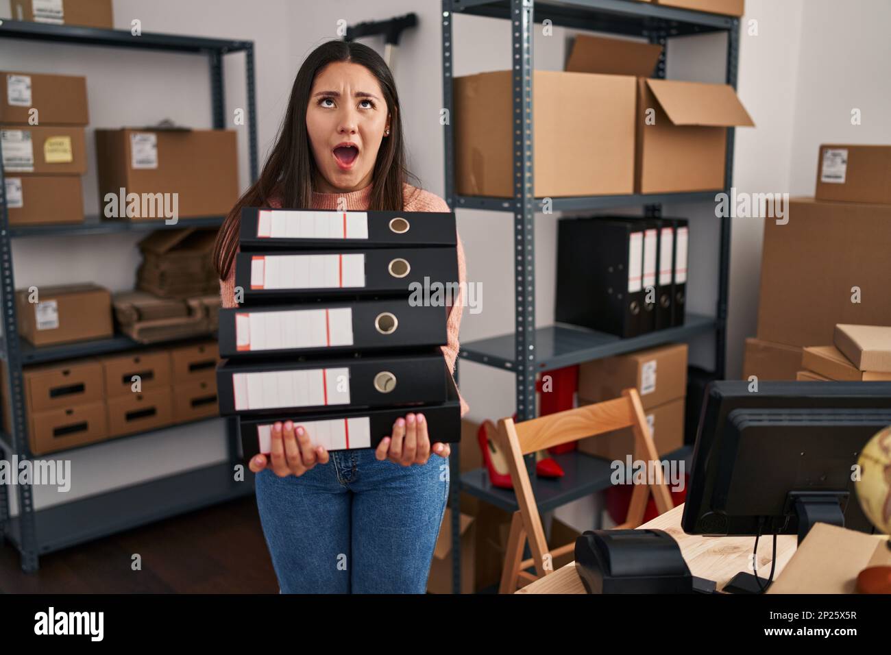 Young latin woman working at small business ecommerce holding folders ...